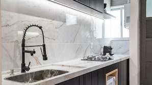 Uma cozinha moderna com armários escuros, bancada de mármore branco e torneira preta.