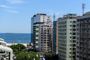 Paisagem urbana com edifícios altos, uma praia e um navio ao longe.