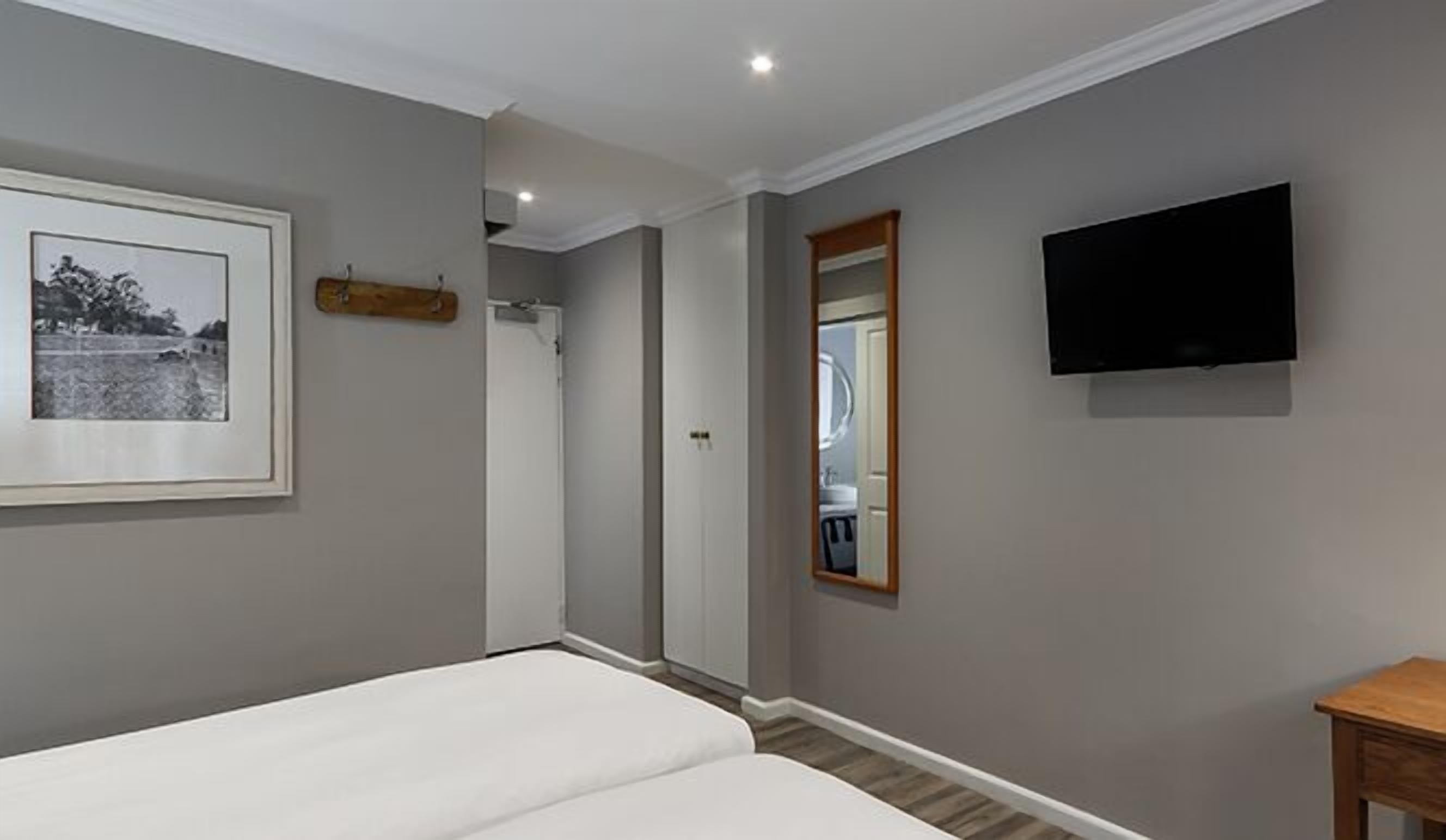 Quarto com cama, televisão na parede, quadro emoldurado e um banco de madeira.