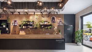 Uma área de recepção moderna com balcão de madeira, várias luminárias pendentes e plantas diversas.