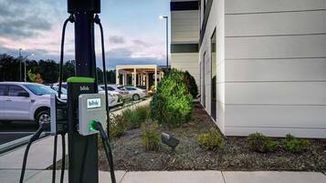 Uma estação de carregamento Blink para veículos elétricos num parque de estacionamento, com um edifício ao fundo.