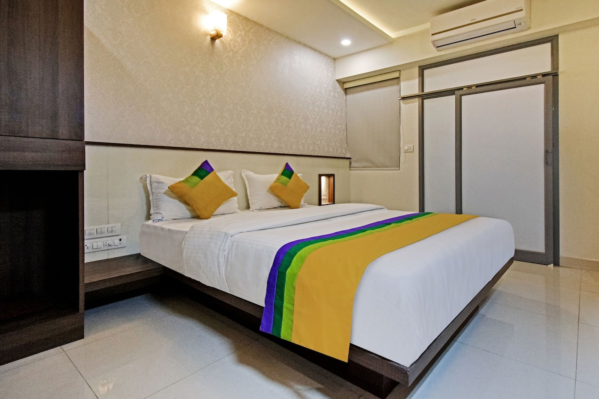 Quarto de hotel com cama, mesa de cabeceira, luminária na parede, aparelho de ar condicionado e uma porta.