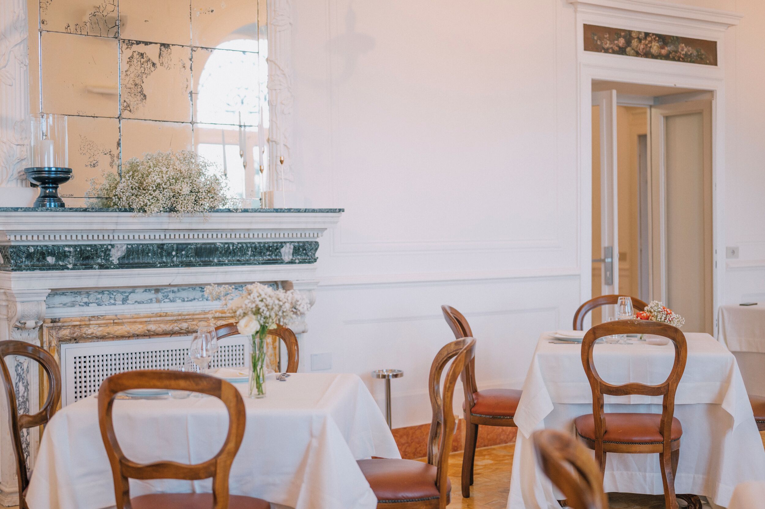 Uma sala de jantar com toalhas de mesa brancas, cadeiras de madeira e uma lareira de mármore.