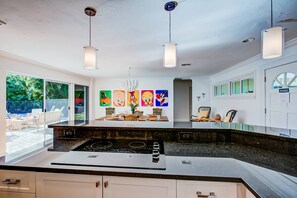 Uma cozinha moderna com ilha central, luminárias pendentes e área de jantar com cadeiras.