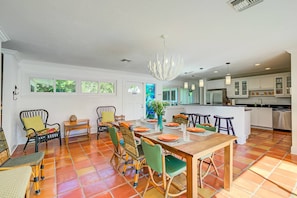 Uma sala de jantar ampla com uma mesa e cadeiras de madeira, uma cozinha com armários brancos e uma janela grande com vista para o verde.