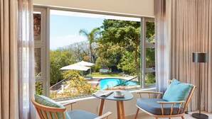 Uma varanda com duas cadeiras de madeira, uma mesa pequena e vista para uma piscina e jardim.