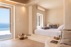 Quarto com cama, janela, cesta de toalhas e vista para o mar.