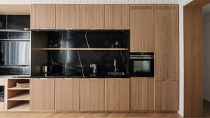 Cozinha moderna com armários de madeira, bancadas de mármore preto e eletrodomésticos embutidos.
