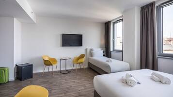 Quarto de hotel com cama, duas cadeiras, televisão e mala.