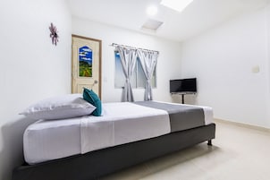 Quarto com cama, televisão, janela com cortinas e porta com quadro.