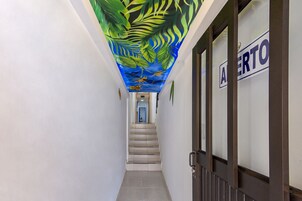 Um corredor com um mural no teto retratando folhas e peixes tropicais, uma escada e uma porta com a inscrição 'ALBERTO'.