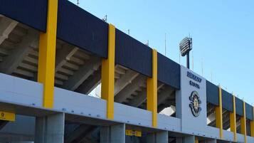 Um estádio com vários níveis de arquibancadas, uma entrada destacada marcada com o número 9, e um grande letreiro iluminado sobre a entrada.