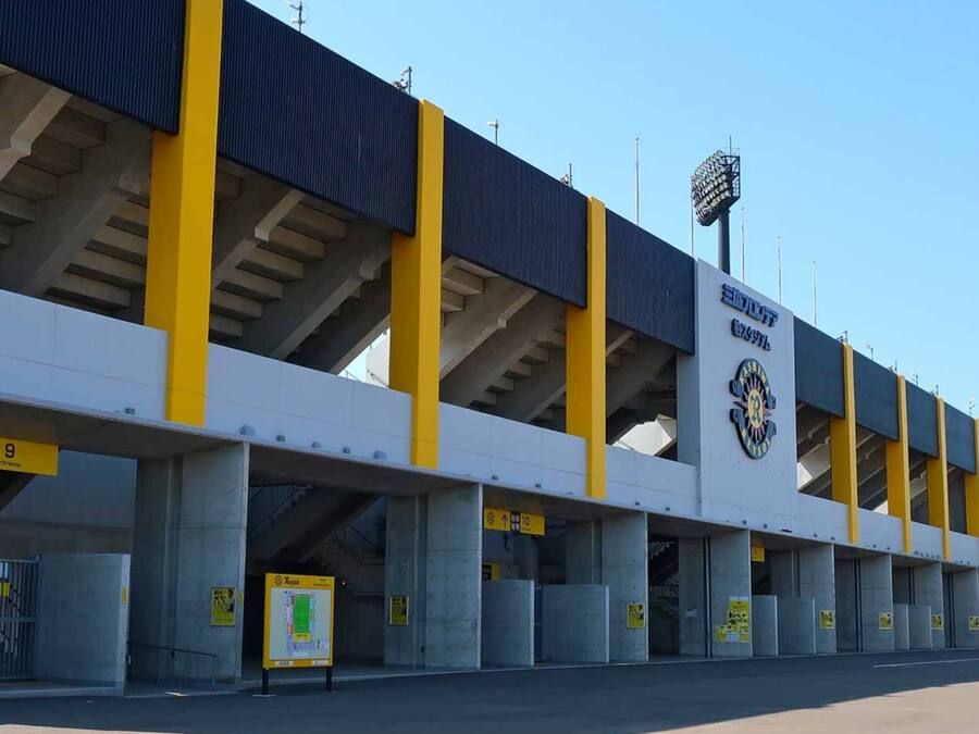 Um estádio com vários níveis de arquibancadas, uma entrada destacada marcada com o número 9, e um grande letreiro iluminado sobre a entrada.