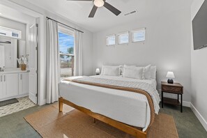 Quarto com cama, mesas de cabeceira, ventilador de teto e vista para o exterior.