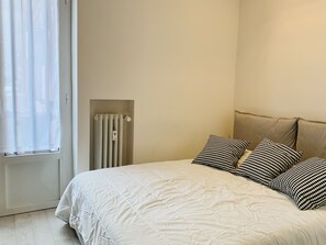 Quarto com cama, radiador e janela com cortinas.