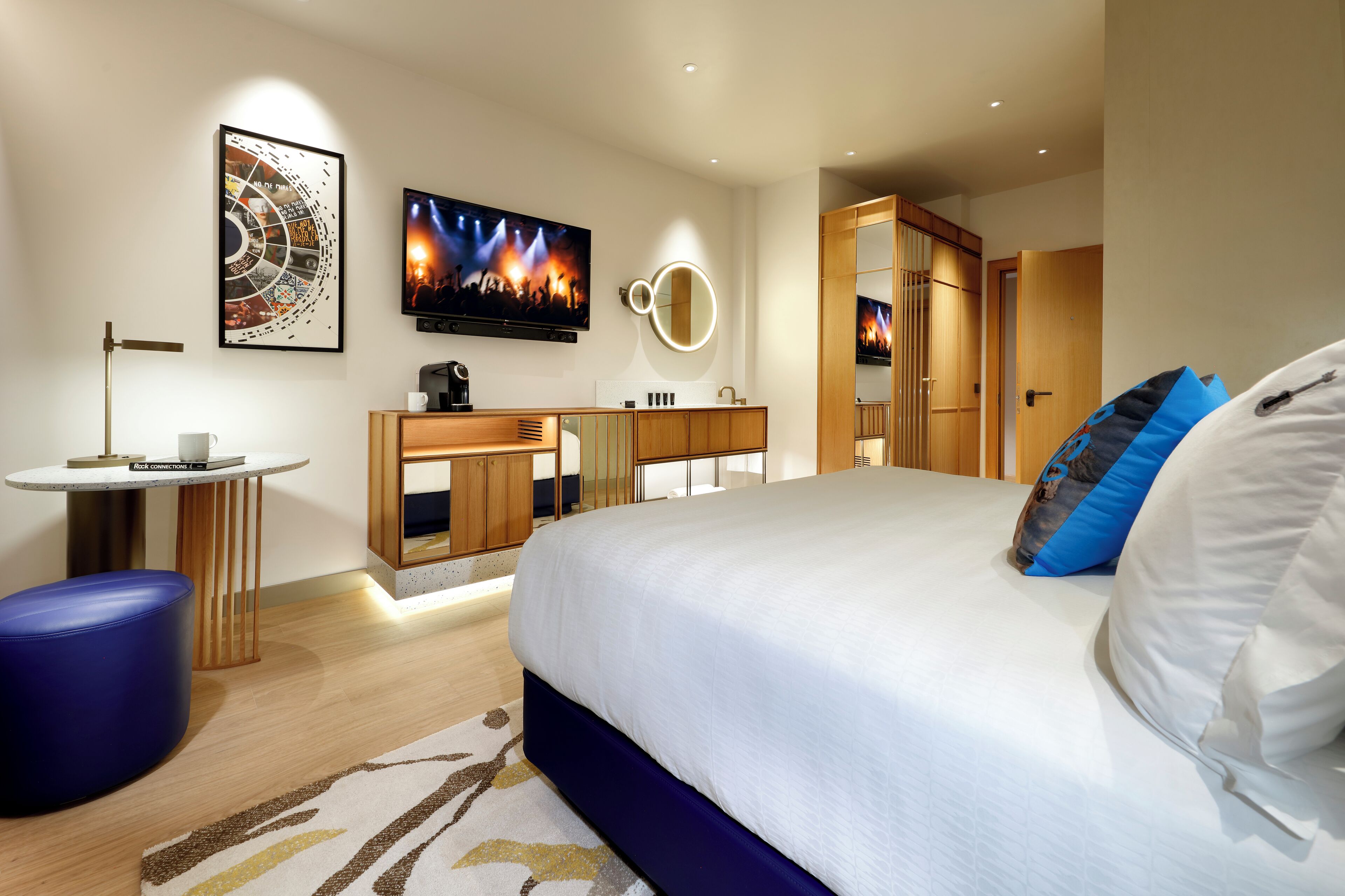 Quarto de hotel moderno com uma cama grande, uma escrivaninha, um espelho e uma televisão na parede.