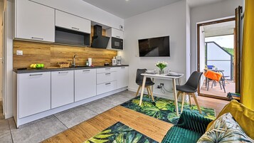 Cozinha moderna com armários brancos, micro-ondas embutido e máquina de café. Há uma área de jantar com mesa, cadeiras e vista para o exterior através de uma porta de vidro.