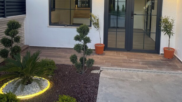 Uma área de recepção moderna com uma placa visível, janelas amplas e plantas em vasos.