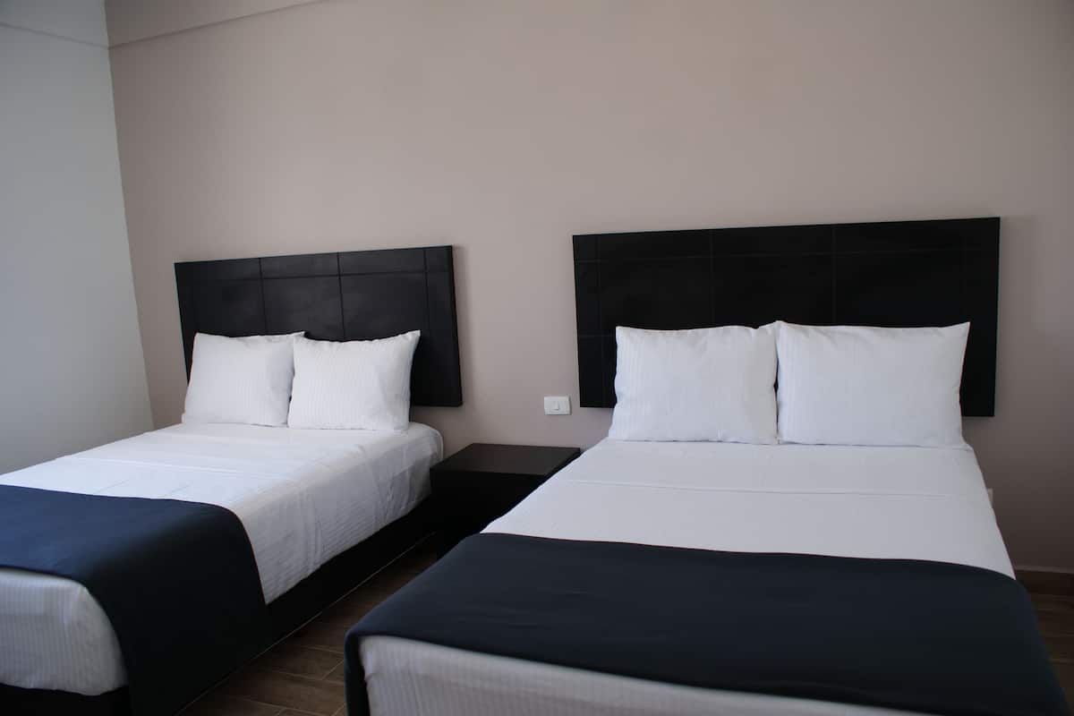 Duas camas de solteiro com cabeceiras pretas e roupa de cama branca em um quarto de hotel.