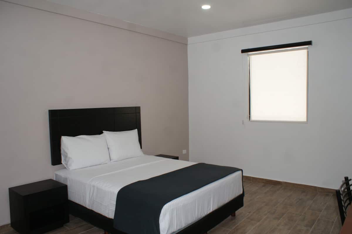 Quarto com cama, mesa de cabeceira, janela e porta.