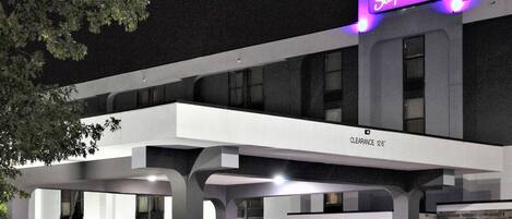 Hotel com letreiro de neon, várias vagas de estacionamento e entrada visível.