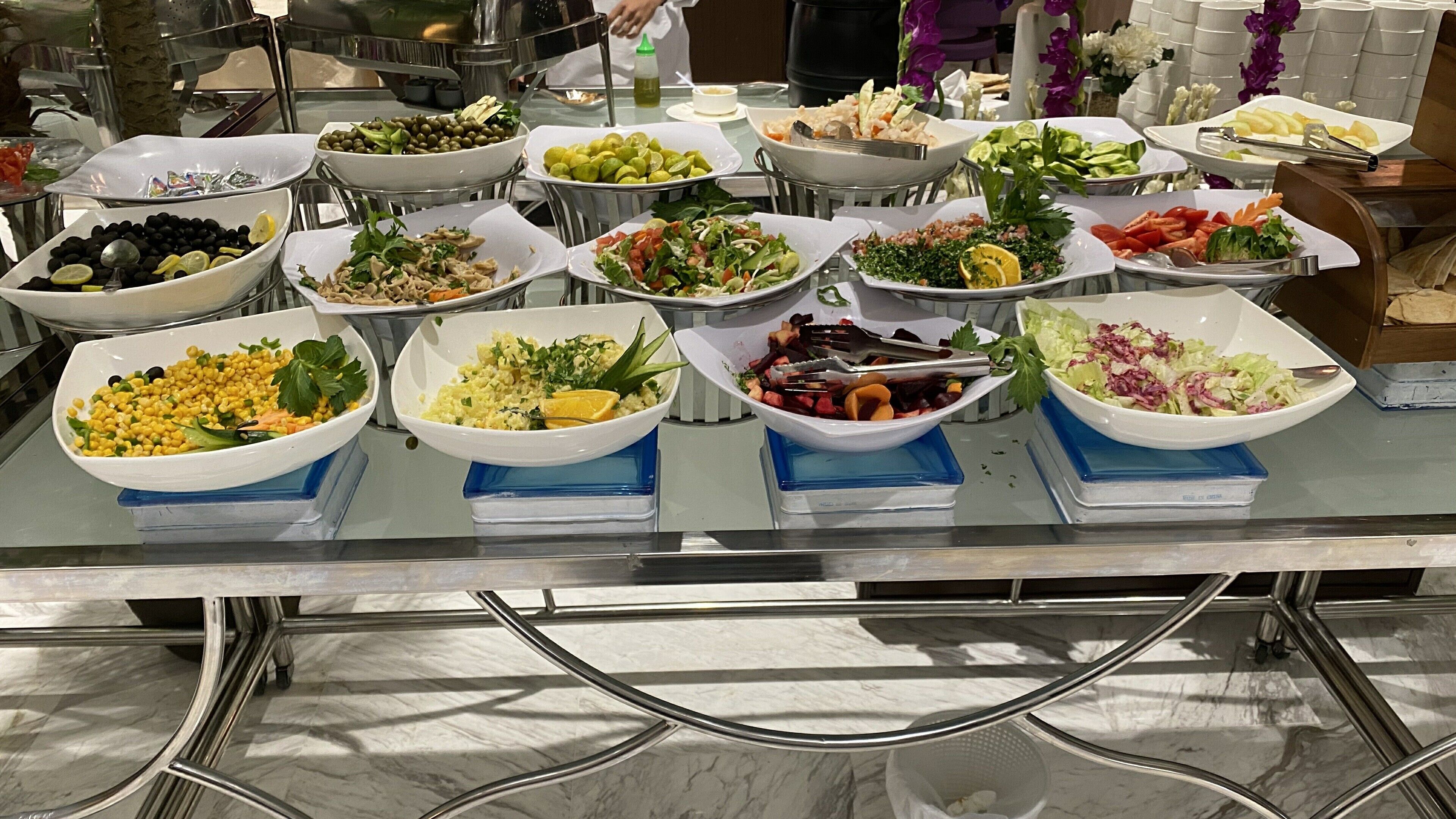 Mesa de buffet com diversos pratos, incluindo saladas, cereais e legumes.