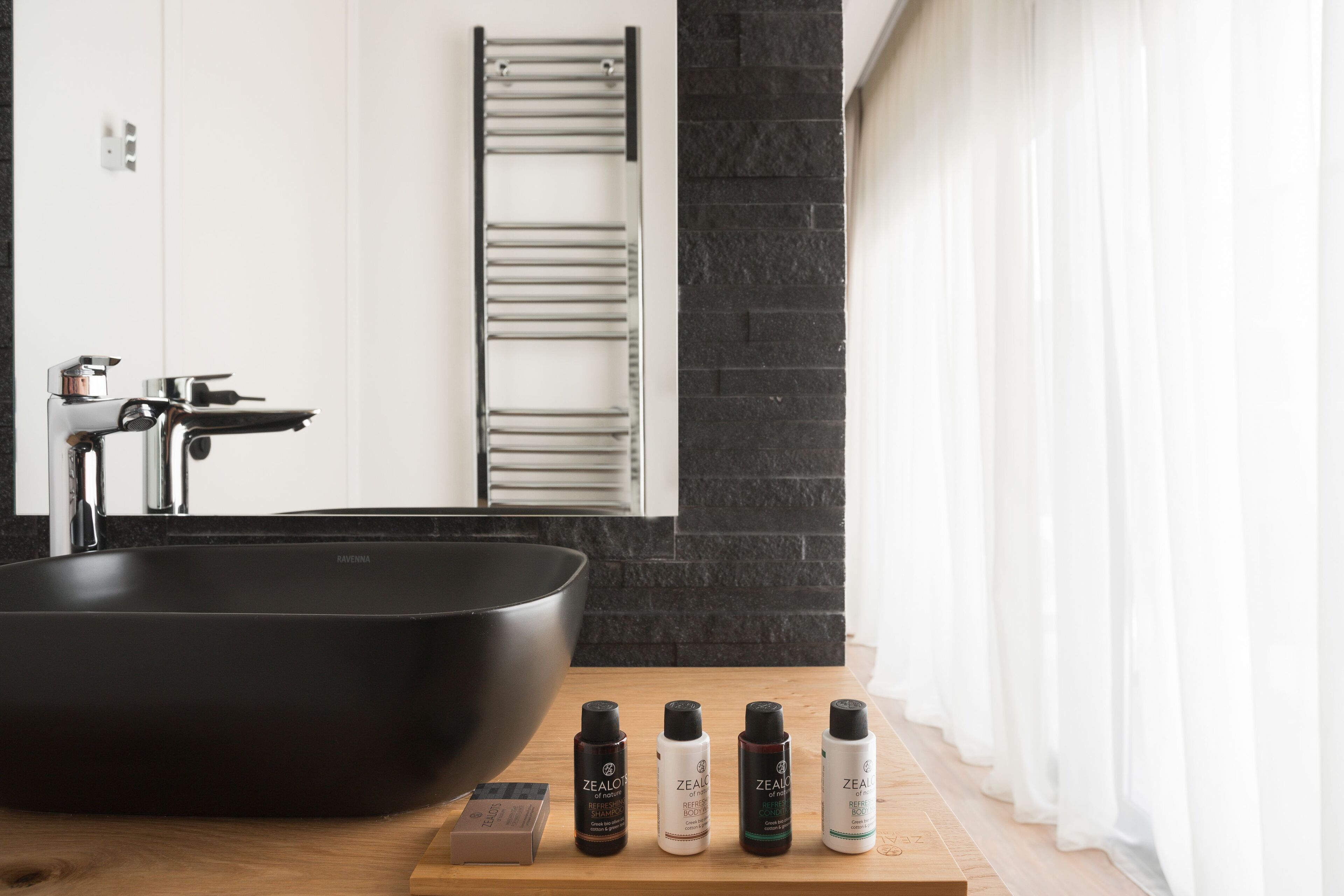 Uma casa de banho moderna com uma lavatório preto tipo cuba, um móvel de vaidade em madeira e quatro frascos de produtos Zeal.