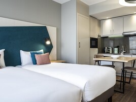 Quarto de hotel moderno com uma cama grande, uma escrivaninha e uma cozinha compacta.