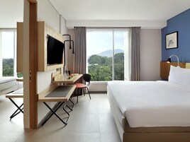 Quarto de hotel com cama, secretária com cadeira, televisão e uma grande janela com vista para as montanhas.