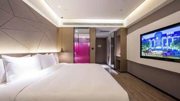 Quarto de hotel moderno com uma cama grande, uma TV de tela plana na parede e vista do exterior do hotel por uma porta de vidro.