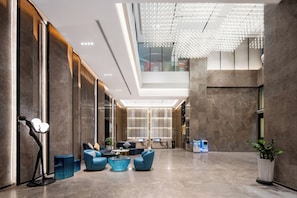 Um lobby moderno com área de estar, balcão de recepção e teto alto com luminária única.