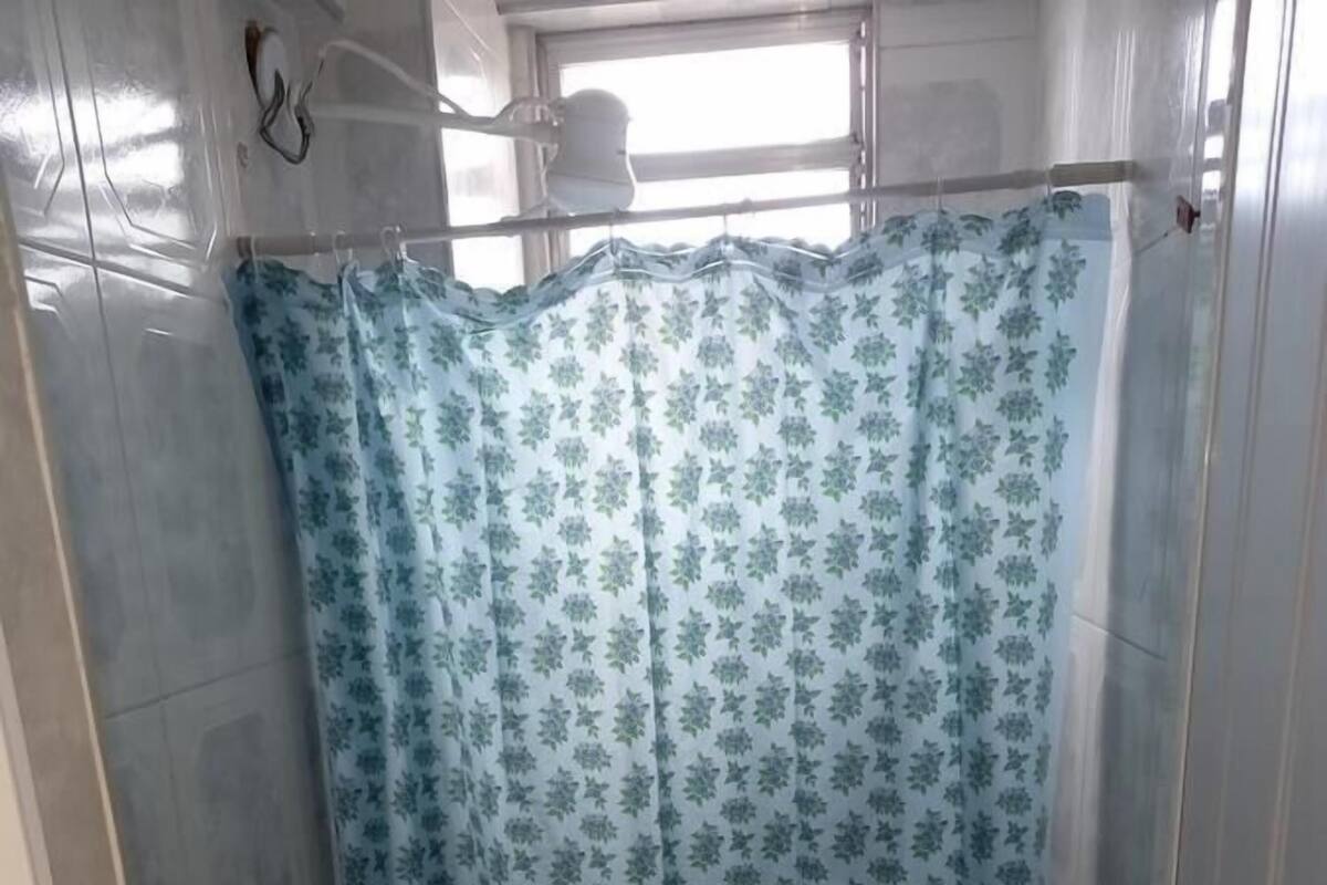 Uma casa de banho pequena com sanita, cortina de chuveiro e suporte para papel higiénico.