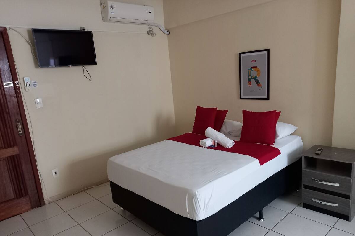 Quarto de hotel com cama, mesa de cabeceira, TV na parede e ar condicionado fixado na parede.