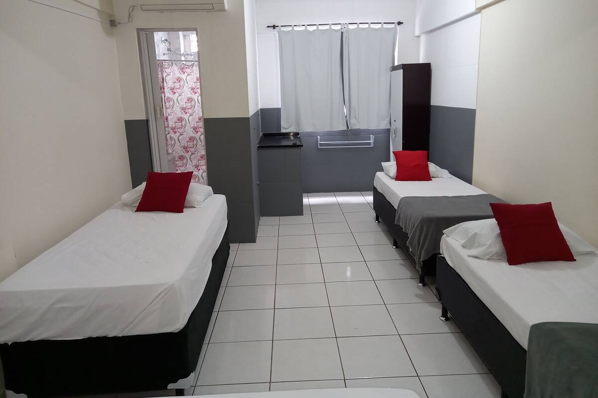 Quarto de hotel com duas camas de solteiro, uma kitchenette pequena e área de chuveiro.