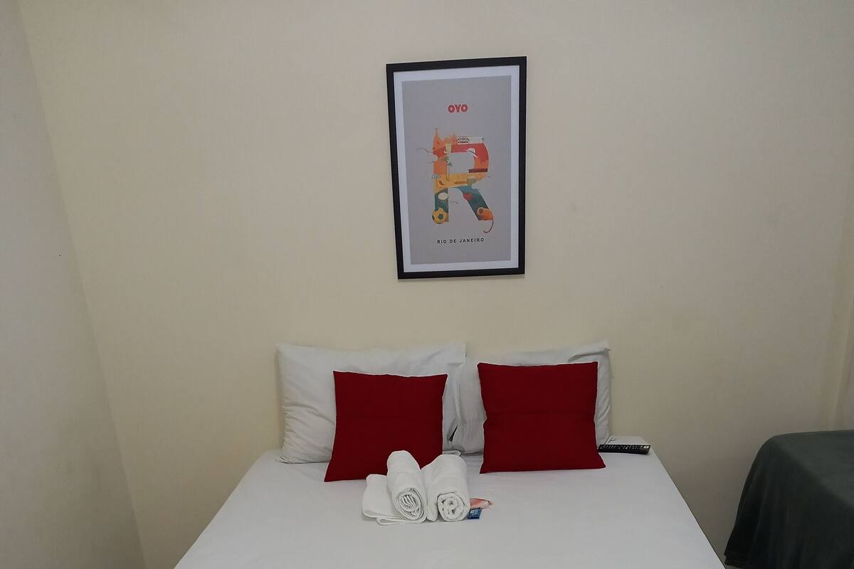 Cama bem arrumada com almofadas brancas e vermelhas, um quadro na parede e estrutura de cama preta.