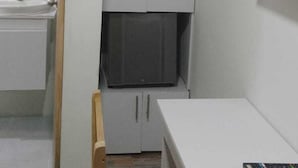Quarto pequeno e compacto com cozinha compacta, uma cama de solteiro e televisão fixada na parede.