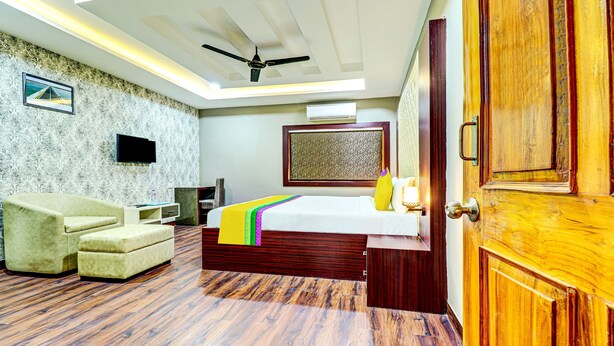 Quarto de hotel com cama, sofá, televisão e ventoinha no teto.