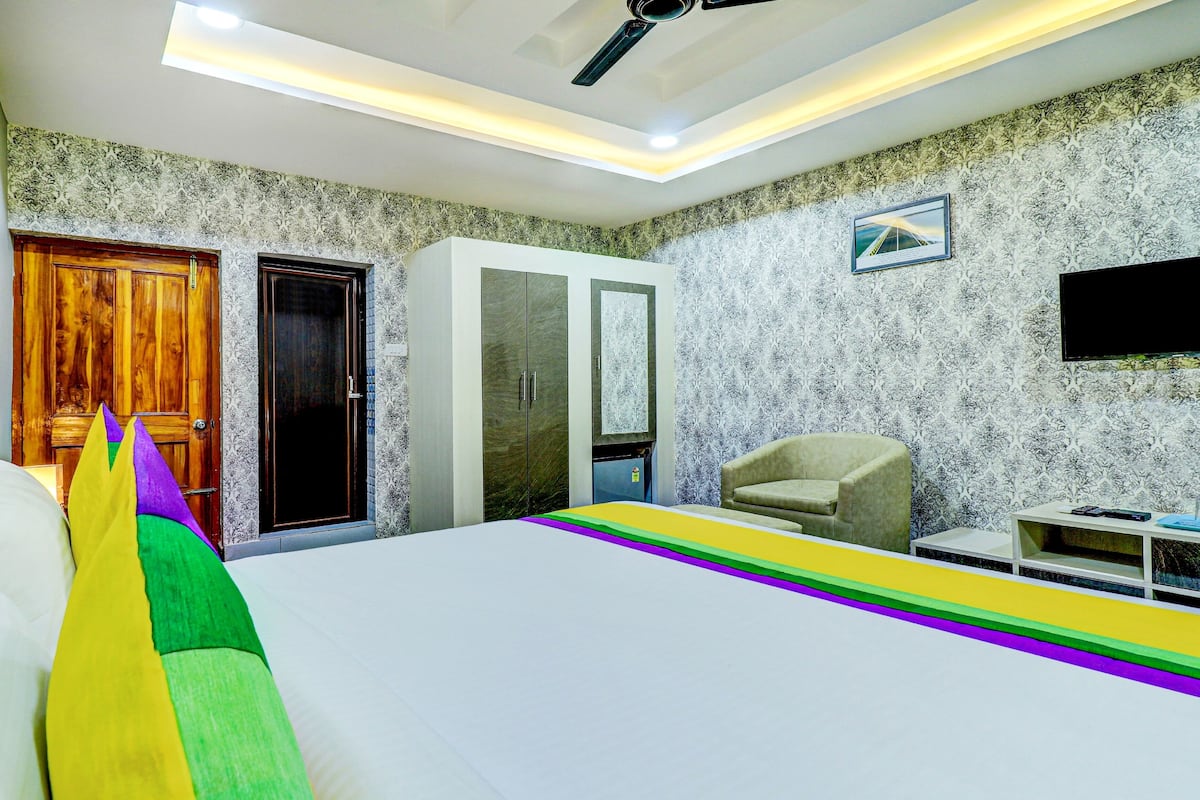 Quarto de hotel com cama, guarda-roupa, espelho, cadeira, televisão e ventoinha no teto.