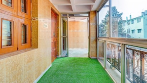 Um corredor com piso verde artificial, portas de madeira e guarda-corpo de vidro com vista para um edifício.