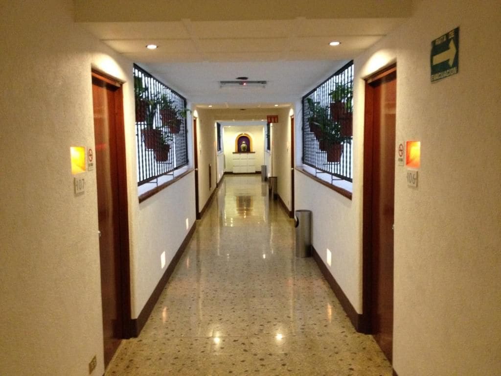 Corredor de hotel com piso lustroso, portas em ambos os lados e placa indicando a direção para o elevador.