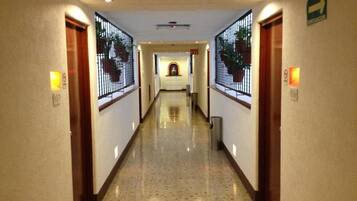 Corredor de hotel com piso lustroso, portas em ambos os lados e placa indicando a direção para o elevador.
