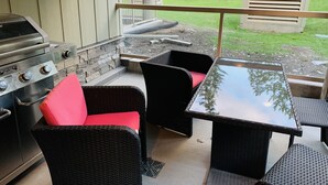 Um pátio externo com churrasqueira, móveis de vime e vista para o quintal.