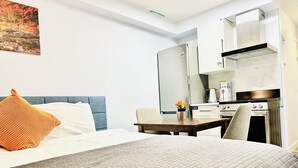 Quarto de hotel com cama, escrivaninha, cadeira, cozinha compacta e um espelho grande.