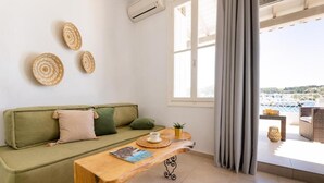 Quarto aconchegante com sofá verde, mesa de centro de madeira e vista para uma varanda com mobiliário exterior.