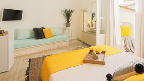 Quarto de hotel com uma cama, um sofá, uma mesinha com bandeja, uma planta em vaso e um espelho.