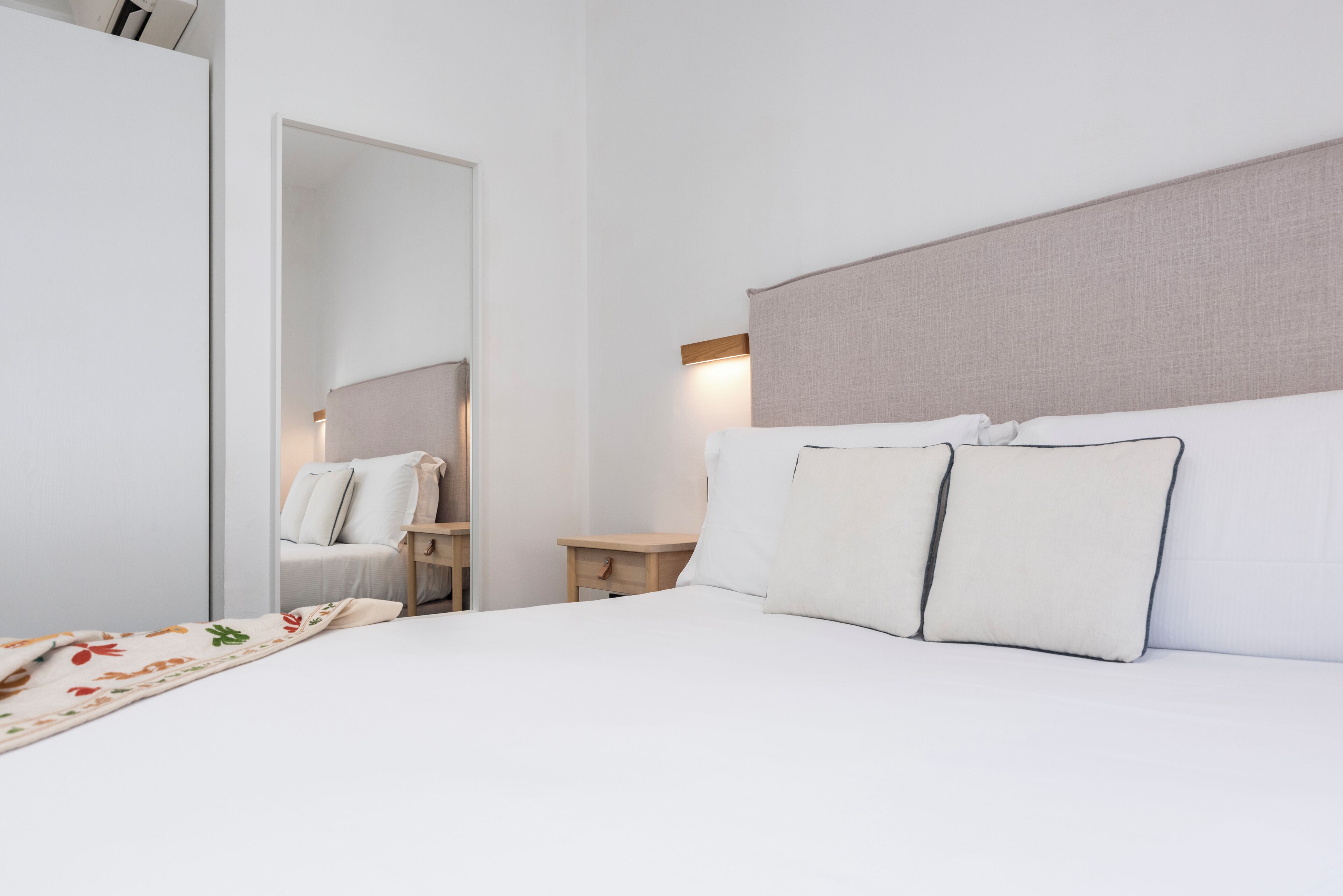 Quarto de hotel moderno com uma cama grande, uma mesinha de cabeceira, um criado-mudo e uma cadeira.