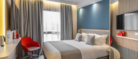 Quarto de hotel moderno com uma cama grande, uma escrivaninha, uma cadeira vermelha e uma televisão.