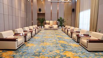 Uma sala de conferências com fileiras de cadeiras, um tapete estampado e um janelão com cortinas.
