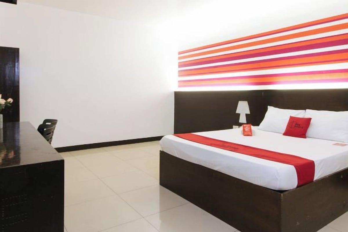Quarto de hotel com uma cama, mesa de cabeceira, luminária e parede com listras horizontais.