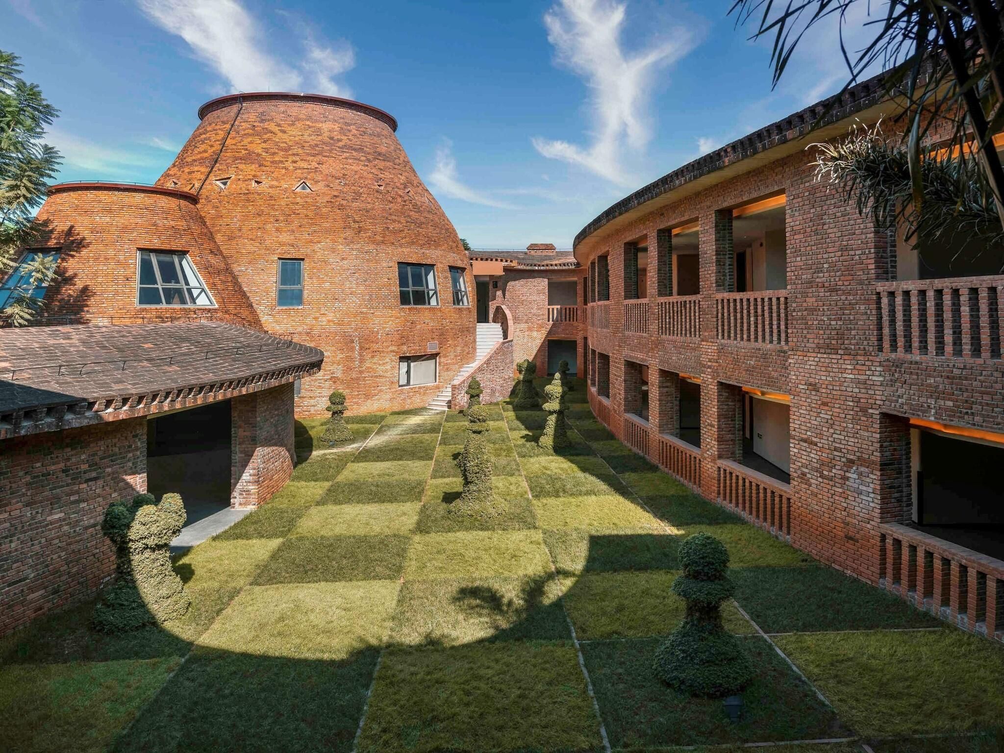 Um pátio com um edifício de tijolos, uma estrutura em cúpula e um gramado bem cuidado.